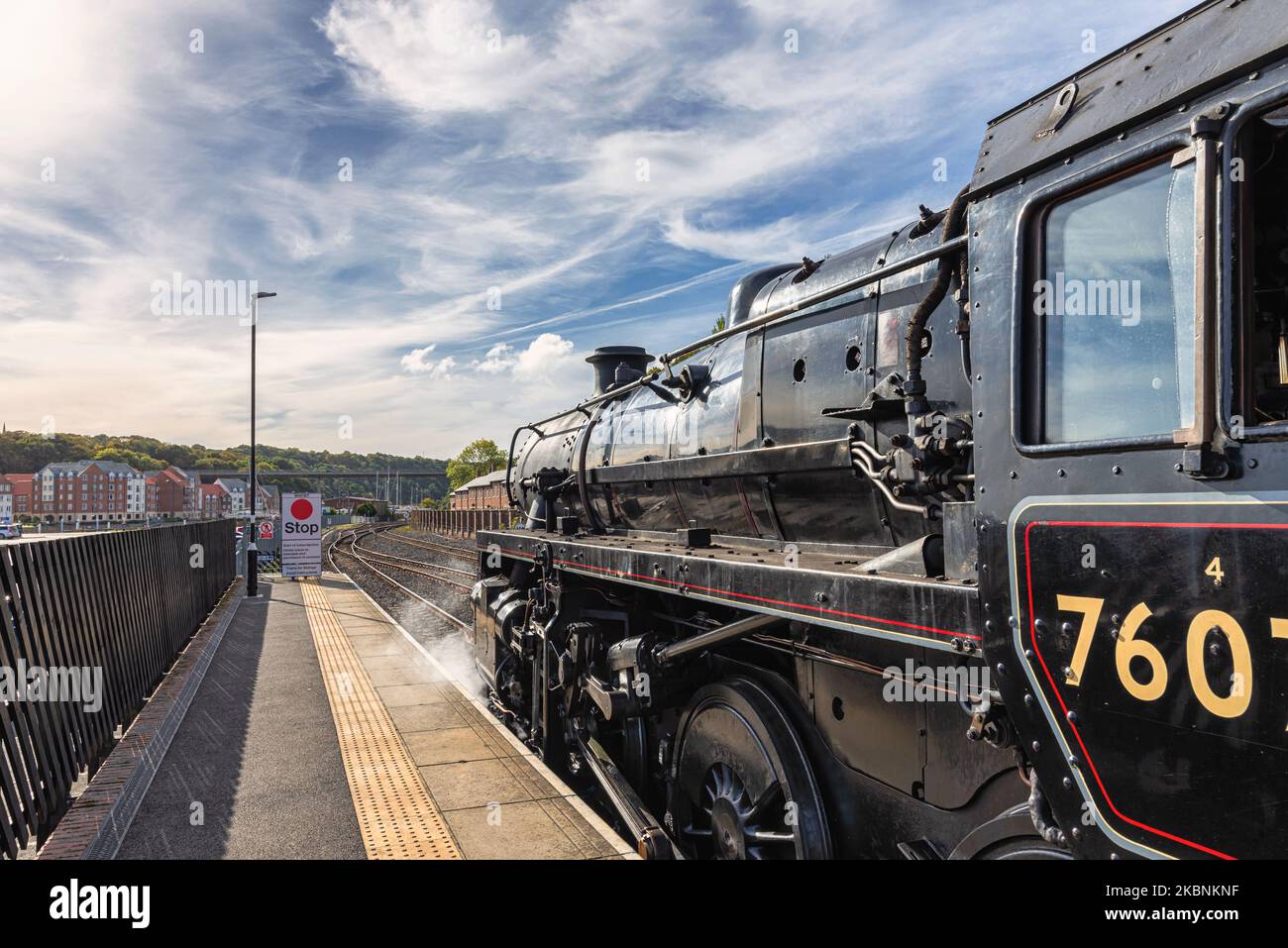 A polished black steam locomotive stands at a platform. Steam emits ...