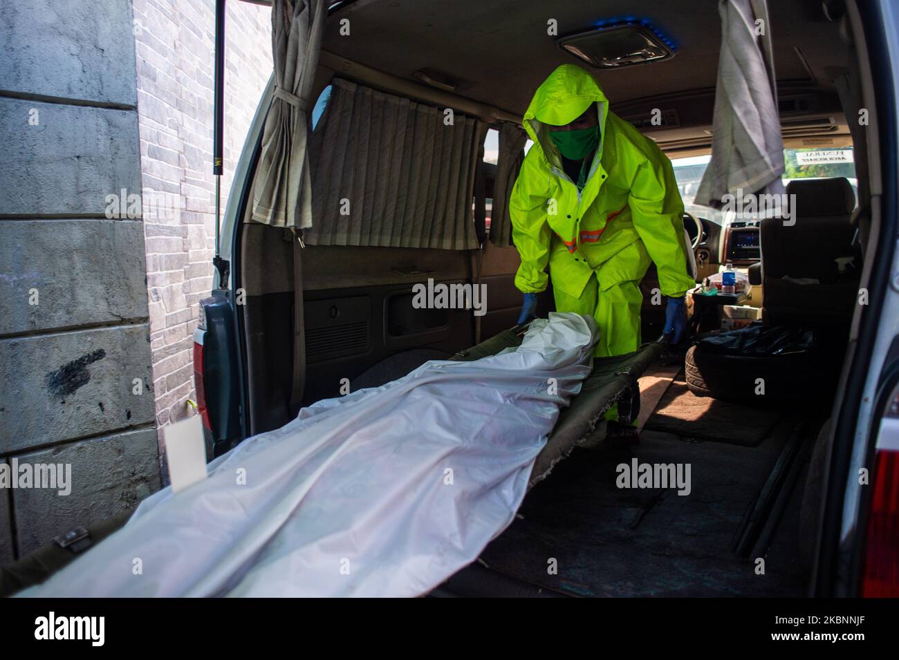 A funeral worker wearing personal protective equipment (PPE) carries a ...