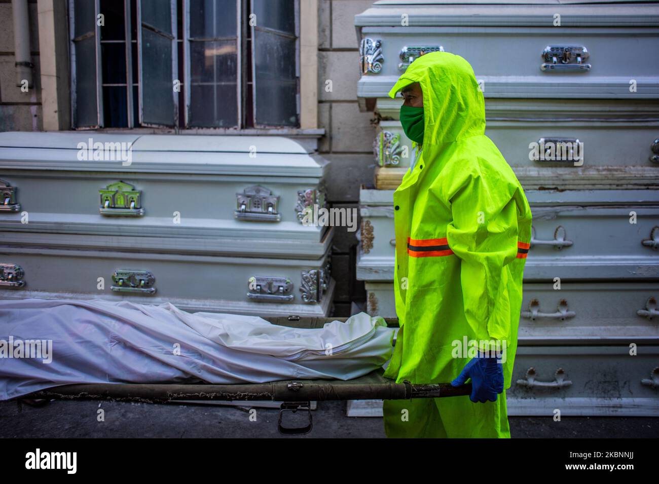 A funeral worker wearing personal protective equipment (PPE) carries a ...
