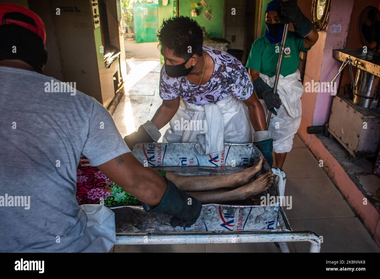 Crematorium workers move a body into a cremation chamber in a ...