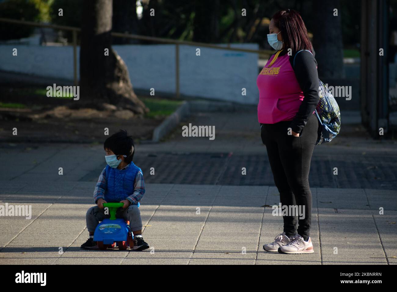 A boy in his toy car, and his mother, stroll through the streets of ...