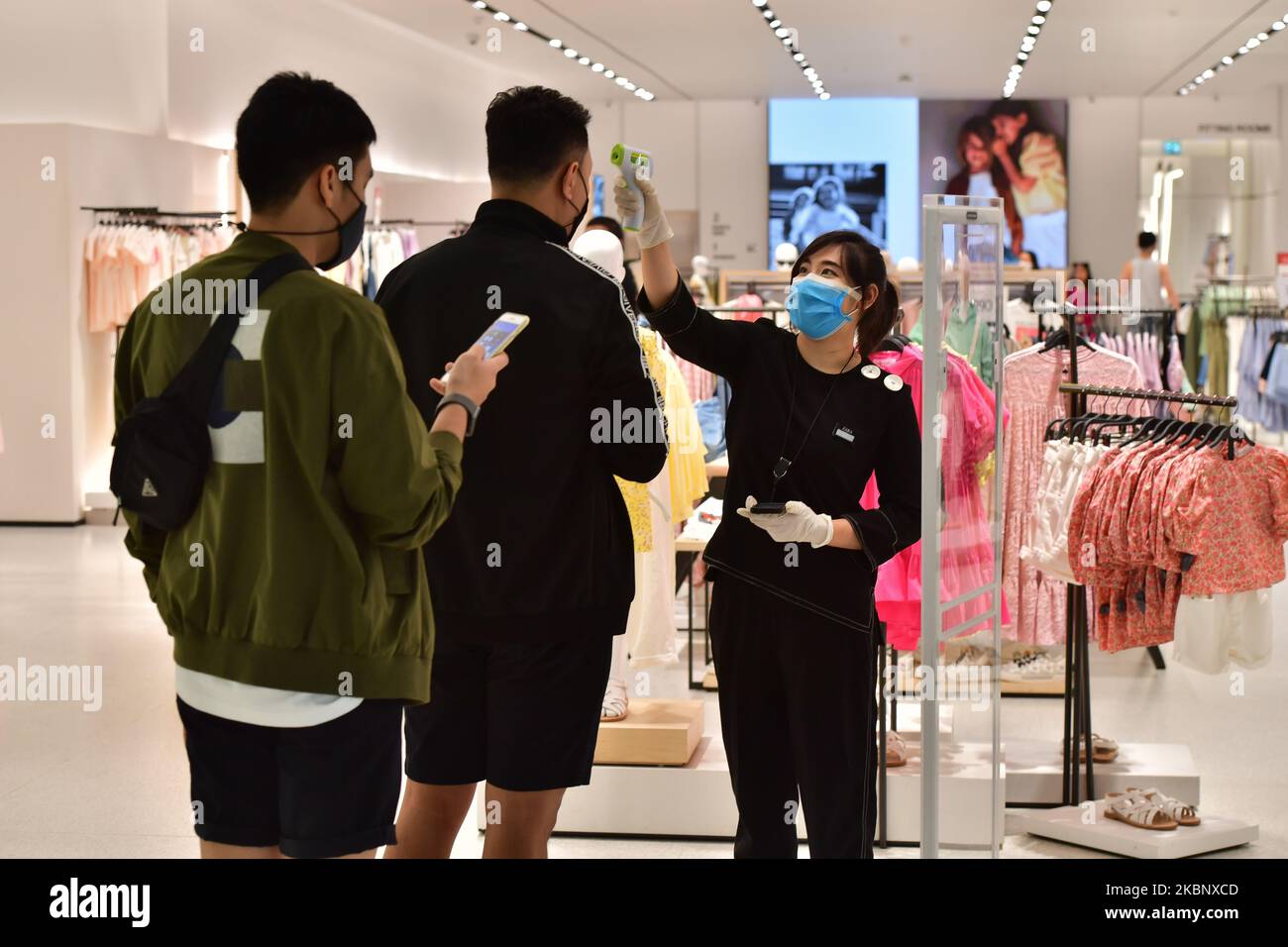 A staff seller wearing a face mask and gloves checks temperature of ...