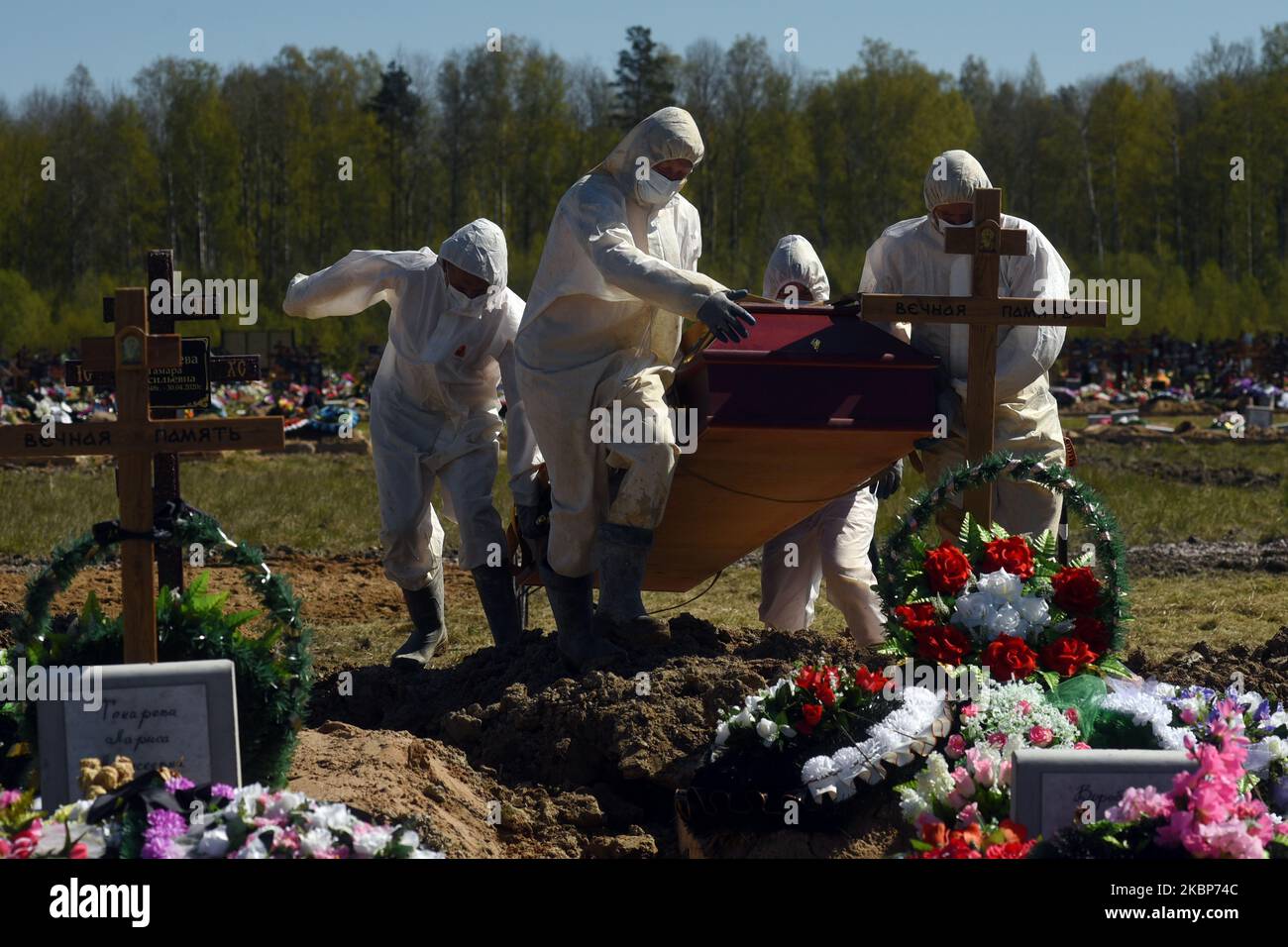 Cemetary employees in chemical protective suits carrying a coffin at ...