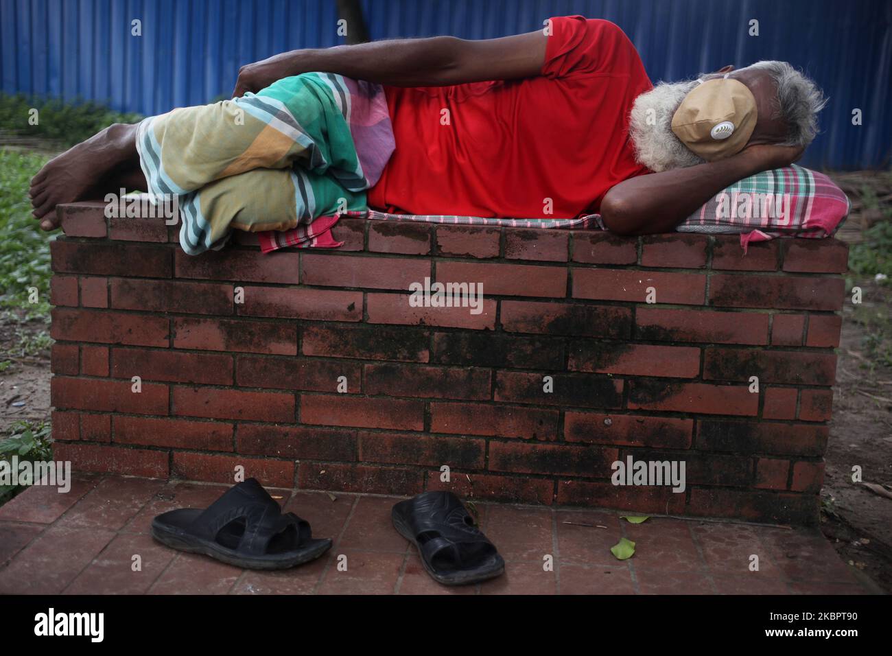 A homeless man covers his face with a mask as he sleeps on a park bench ...