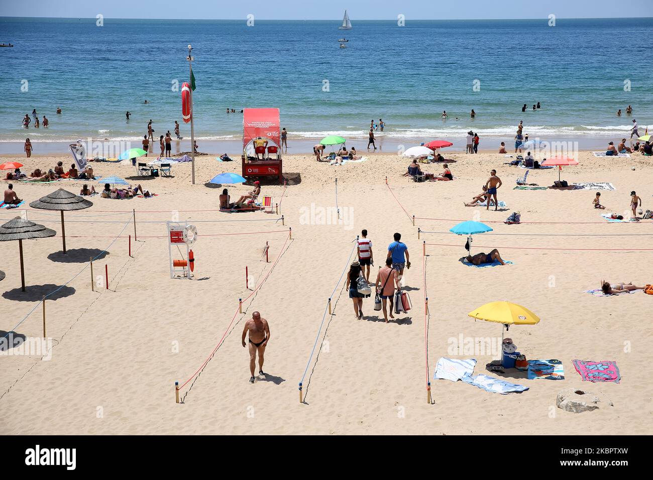 People walk in corridors defined by ropes at the Carcavelos beach in ...