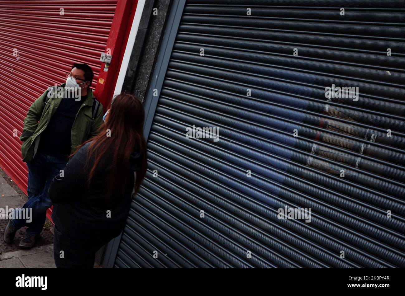 People wearing face masks stand beside shuttered stores on Kilburn High ...