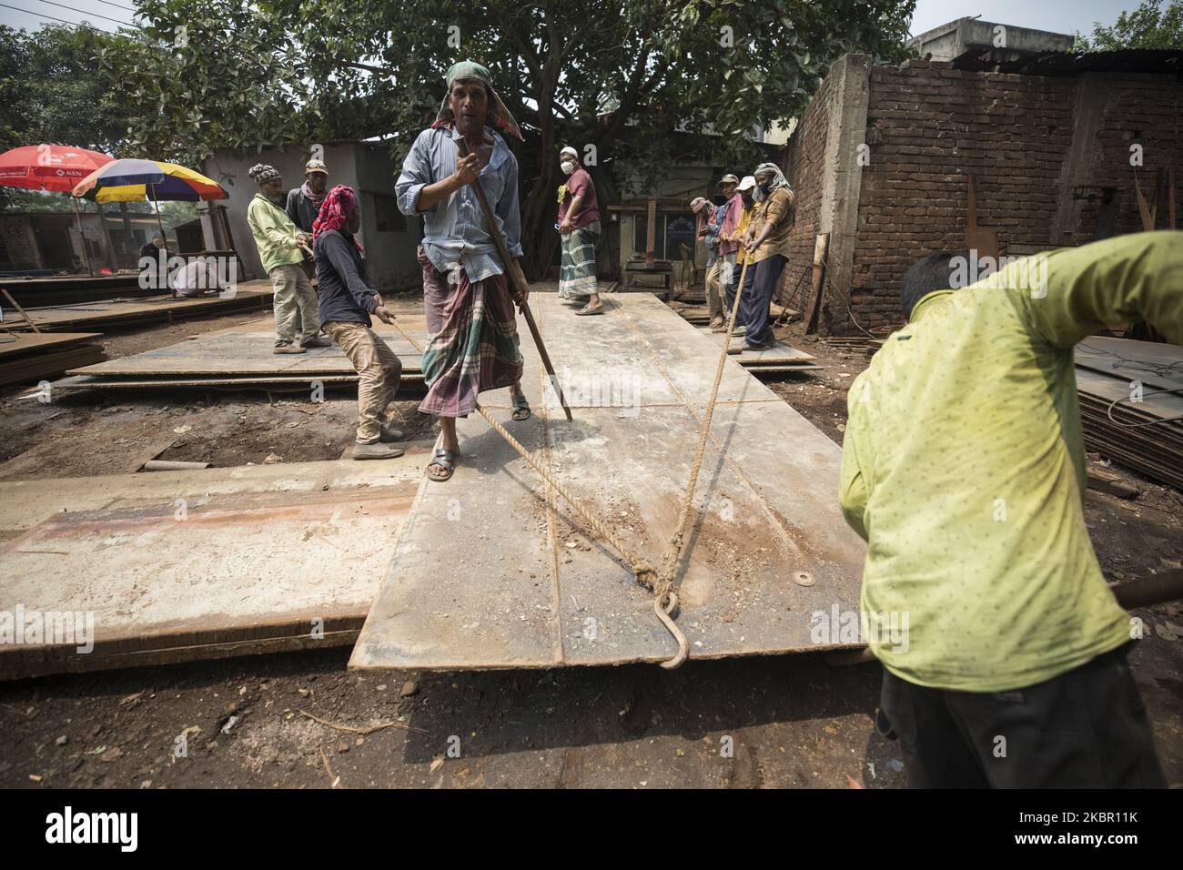 Workers, without wearing face masks and safety gear, pull a metal sheet ...