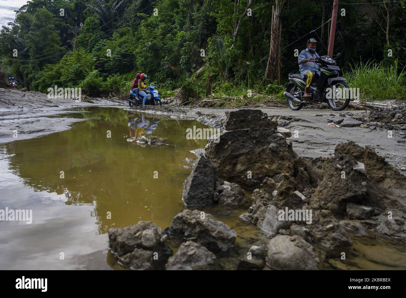 Motorcycle riders cross the road that has been cleared of mud due to ...