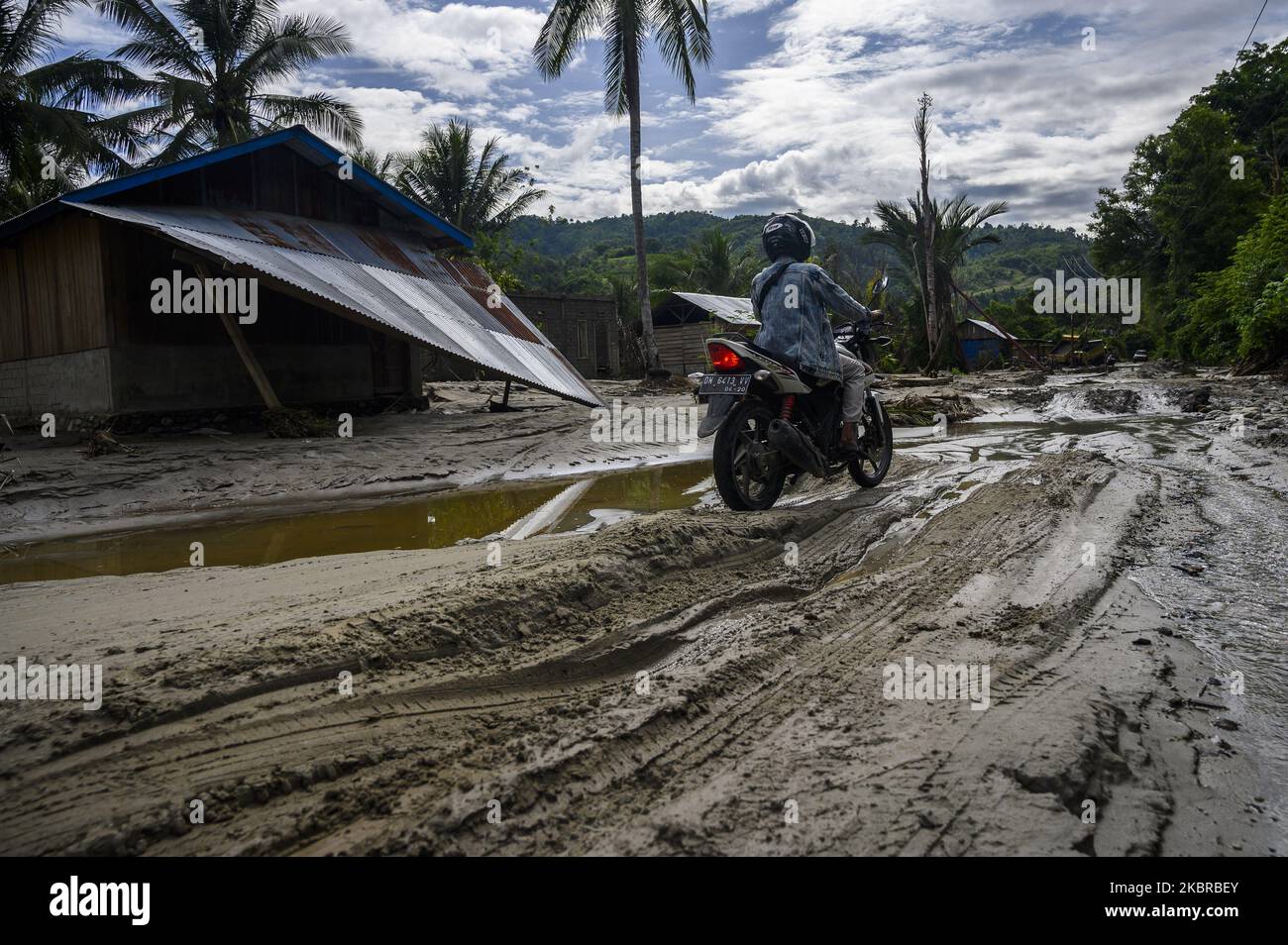 A motorcyclist crosses a road cleared of mud from a flood and landslide ...