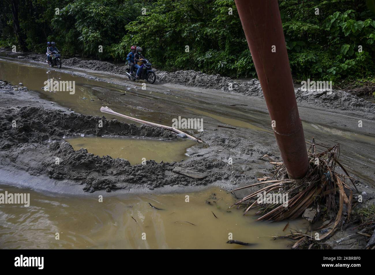 Motorcycle riders cross the road that has been cleared of mud due to ...