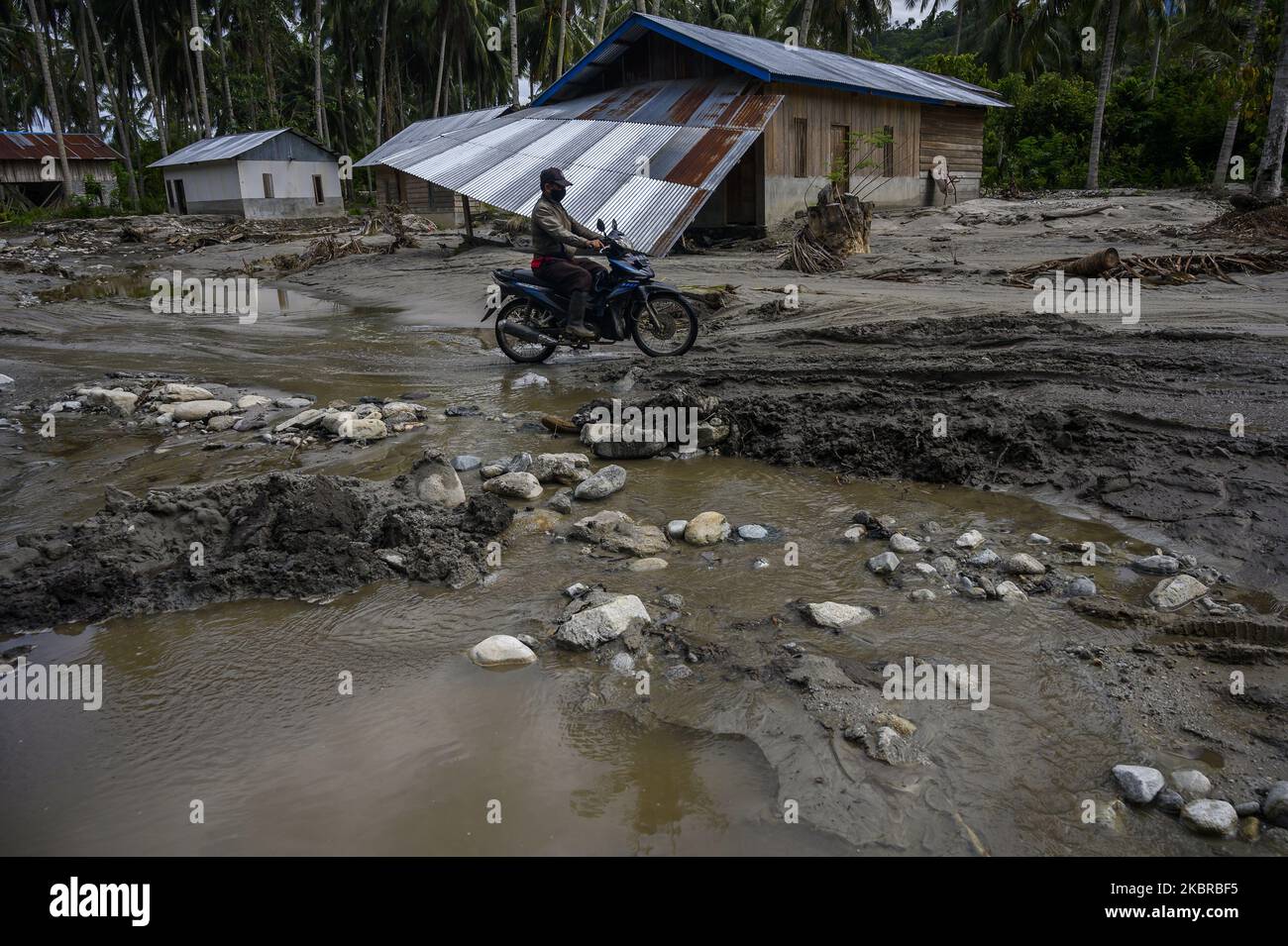 A motorcyclist crosses a road cleared of mud from a flood and landslide ...