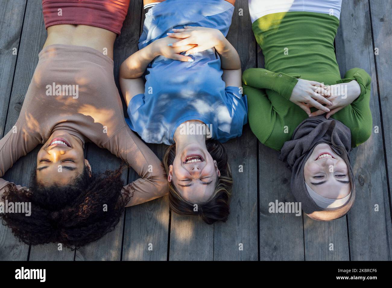 Multiracial young teen female friends resting in the park after sport training laughing and ...