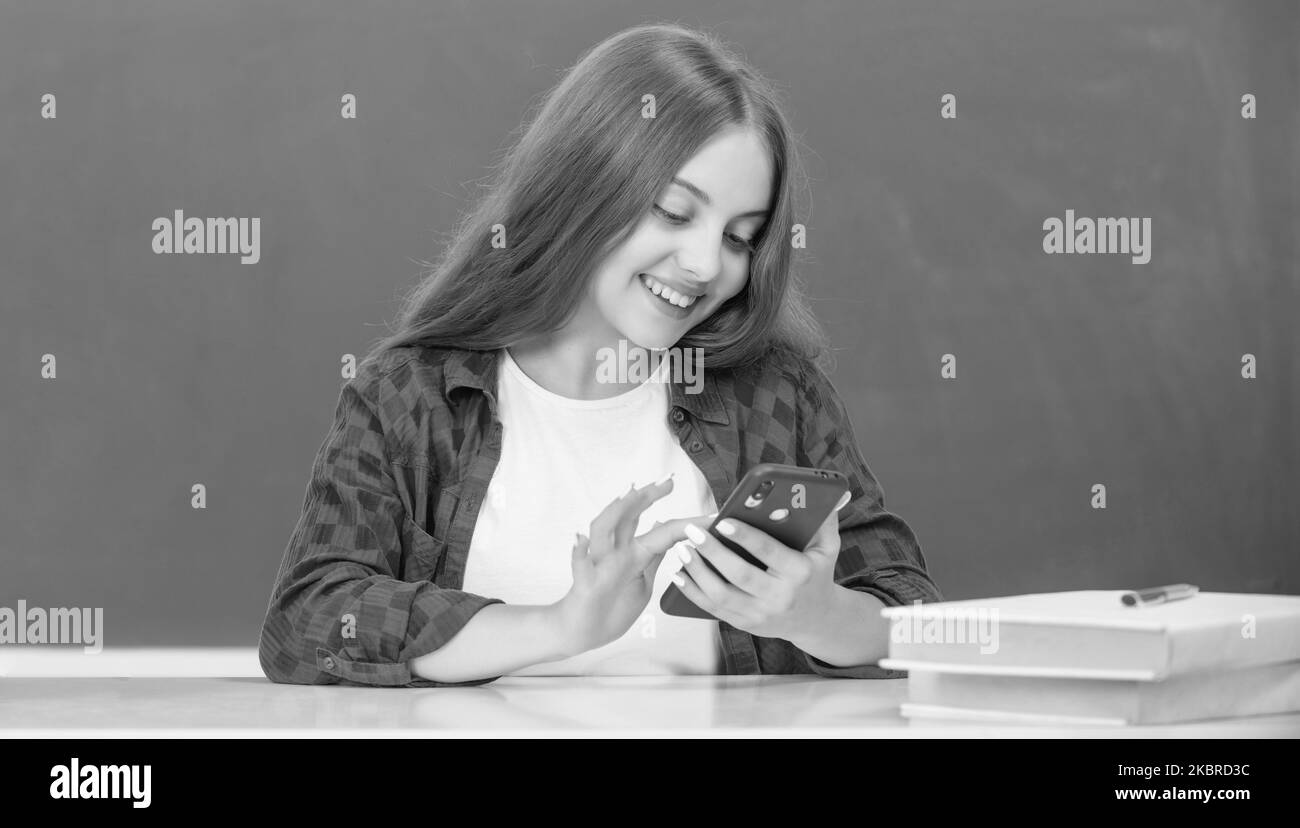 happy kid chatting on smartphone in classroom at blackboard ...