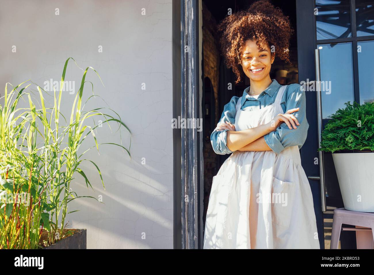 Cafe owner standing in the doorway of her coffee shop. Cheerful young ...