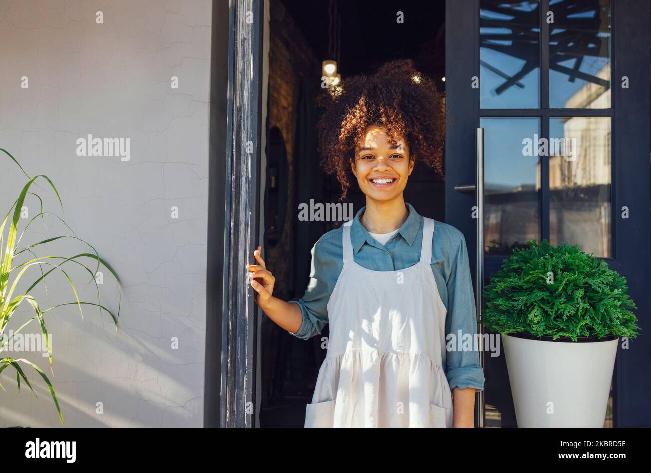 Cafe owner standing in the doorway of her coffee shop. Cheerful young ...