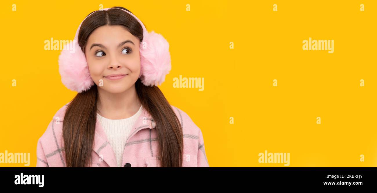 Happy girl child in warm winter fur earmuffs smile with sly look yellow ...