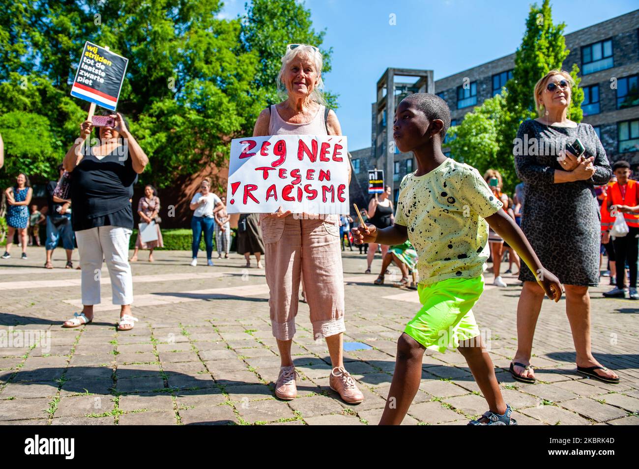 An old white woman is holding a placard against racism while a black ...