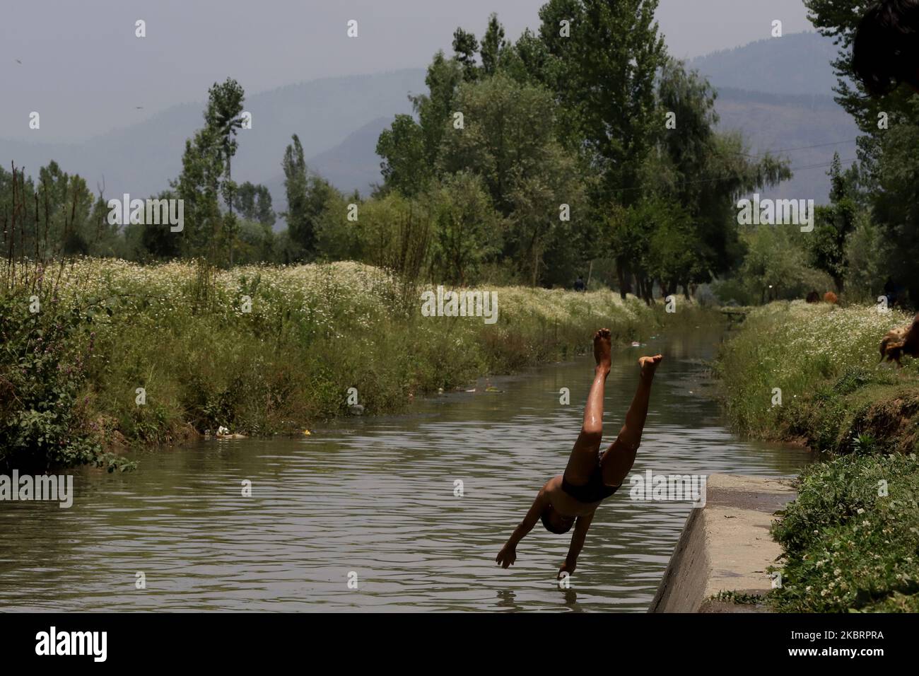 A boy jumps into a stream on a hot summer day in Sopore town of ...
