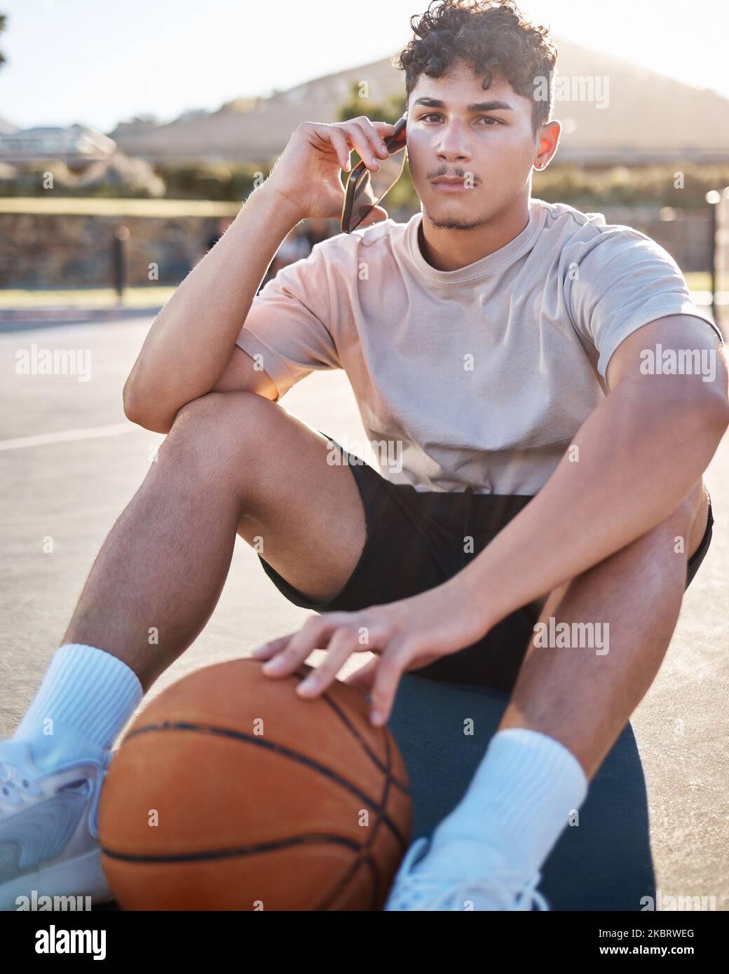 Basketball player, phone call and relax outdoor on floor talking ...