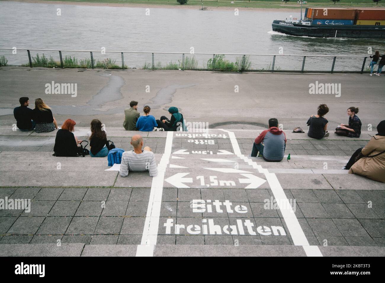 people sit on the stairway which marks the social distance markings in ...
