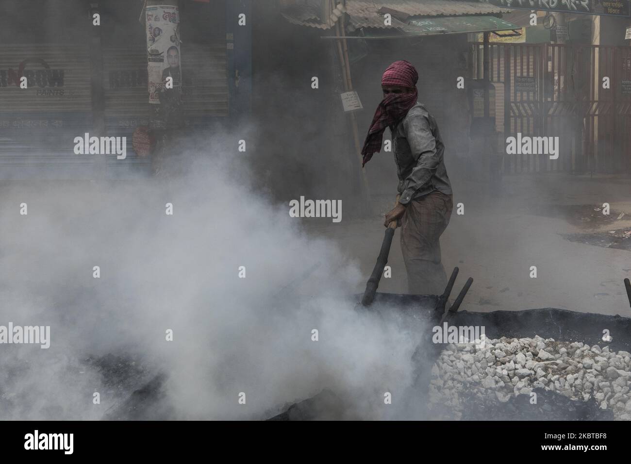 A worker prepares bitumen and rock mixtures to be used to repair a road ...