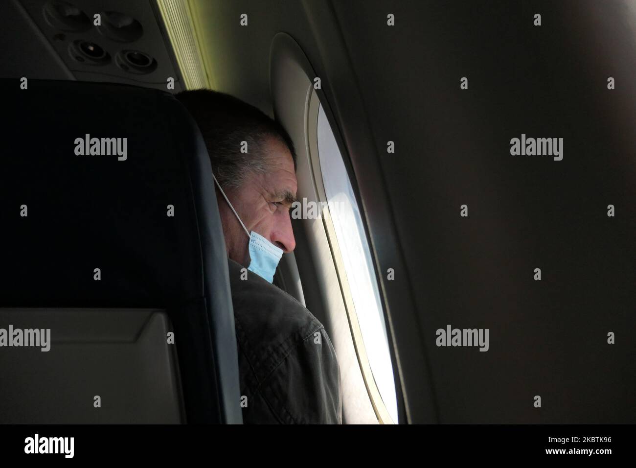 Portrait of a male passenger with a facemask looking out of the window ...