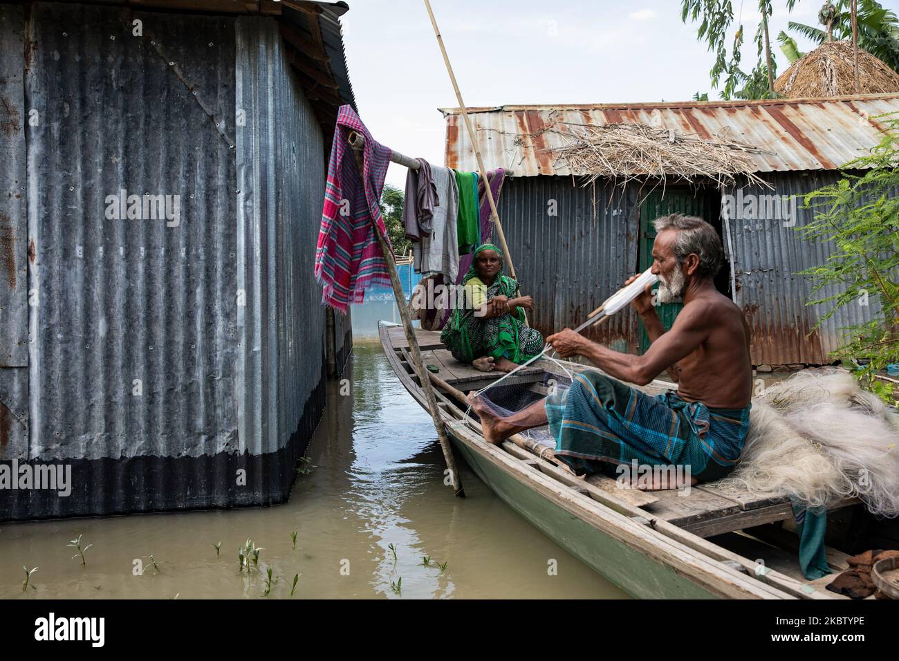 A flood-affected man knits a fishing net while sitting on a boat in ...