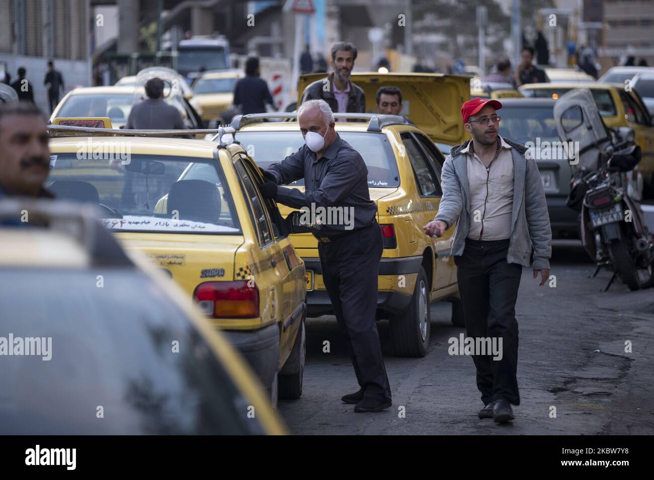An Iranian taxi driver wearing a face mask stands next to his vehicle ...