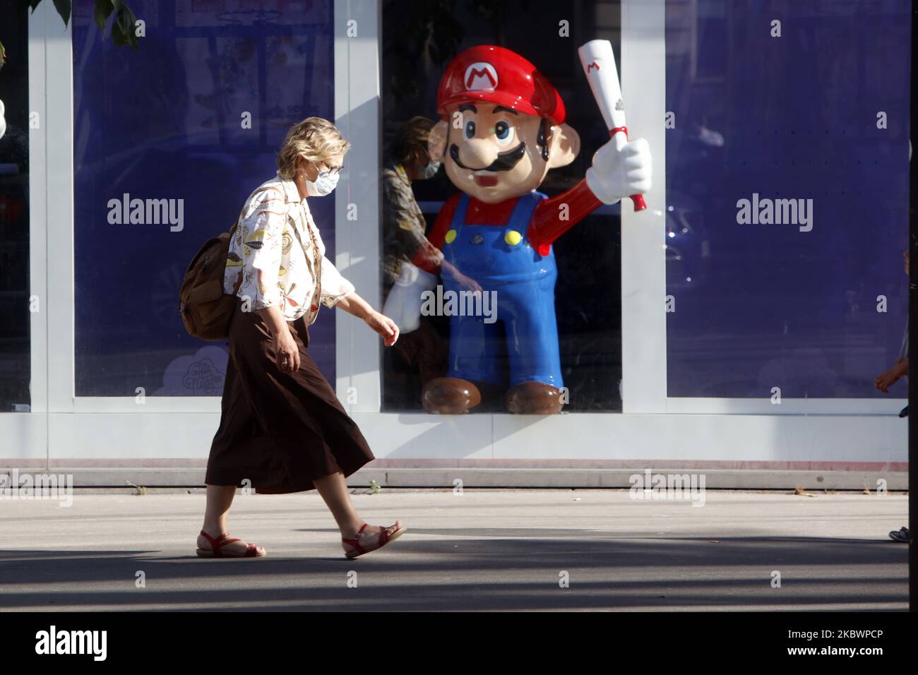 People wearing a protective mask walking a front Mario and Luigi statue ...