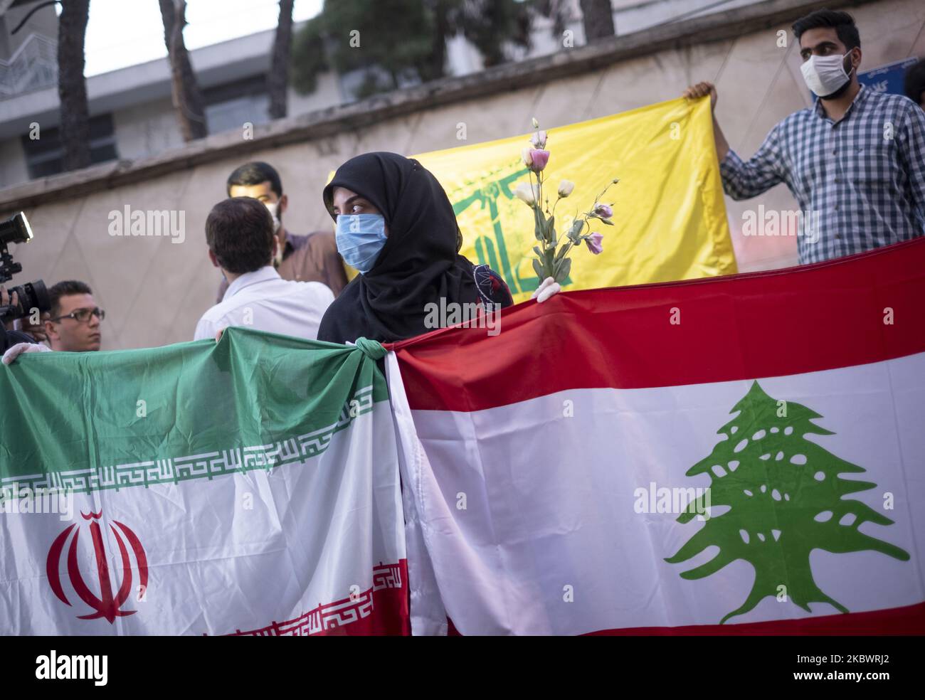 An Iranian woman wearing a protective face mask holds an Iran and ...