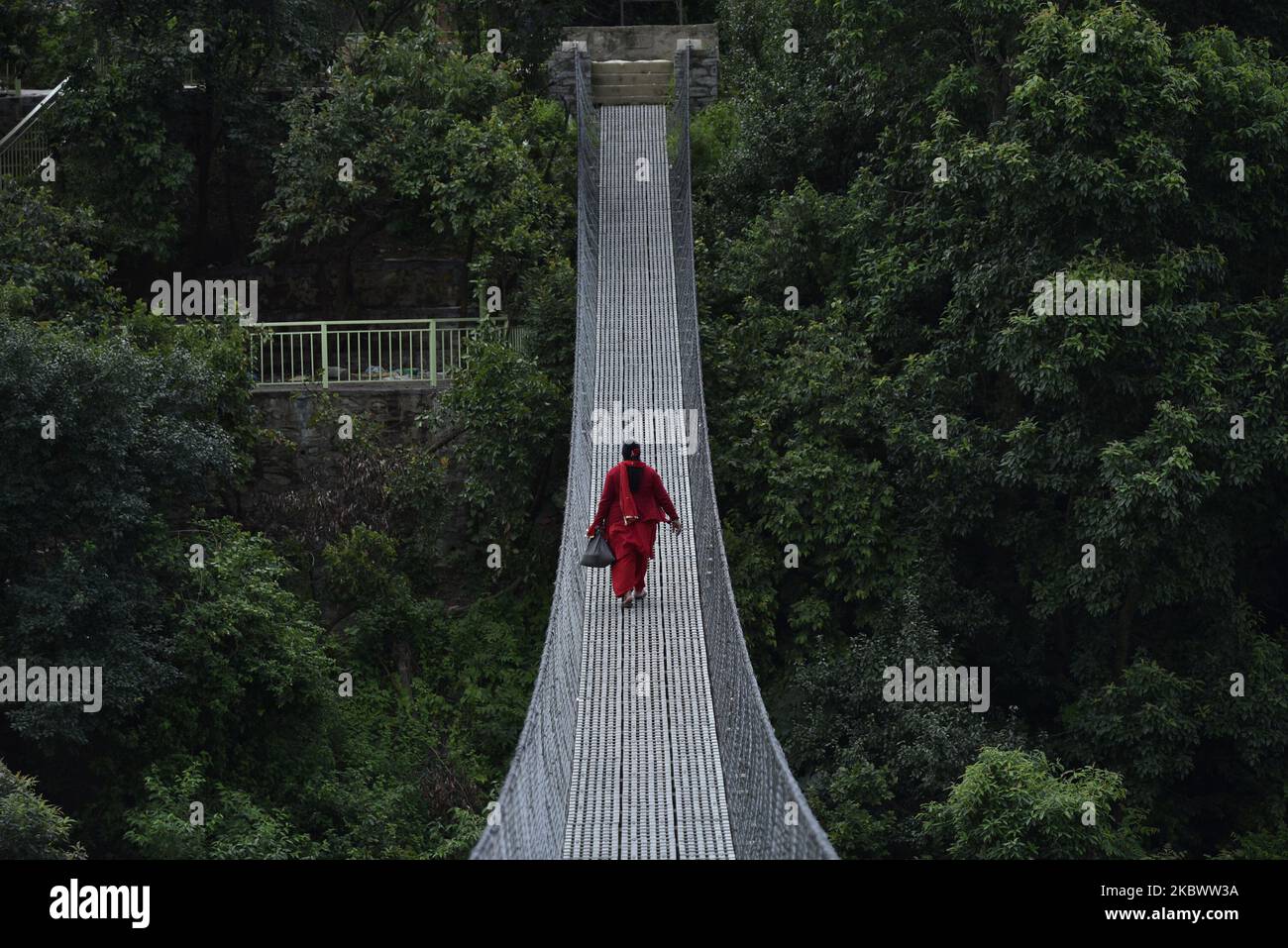 A Nepalese woman alking through a suspension bridge at Kirtipur ...