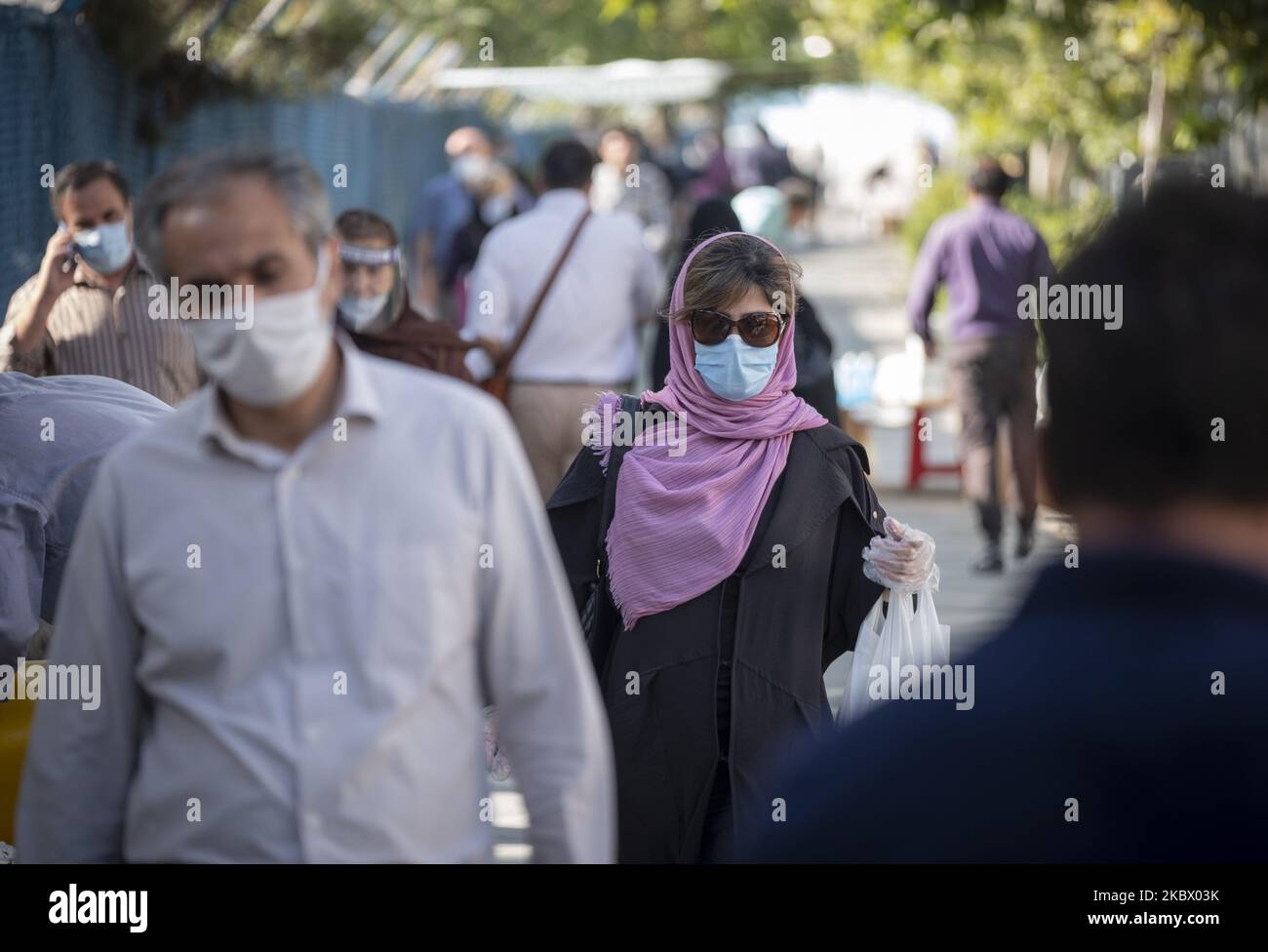 An Iranian woman wearing a protective face mask walks along an avenue ...