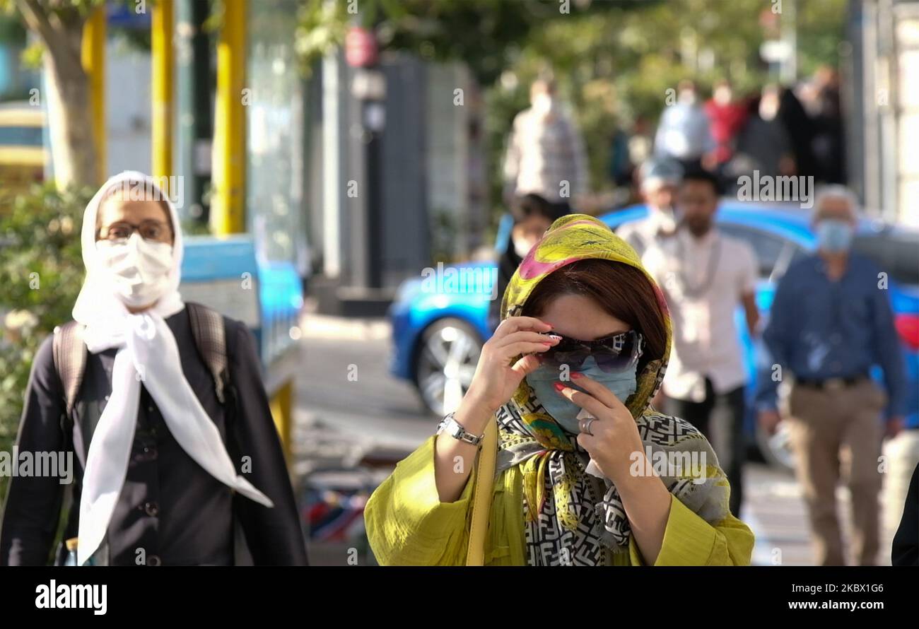 An Iranian woman adjusts her protective face mask while walking along ...