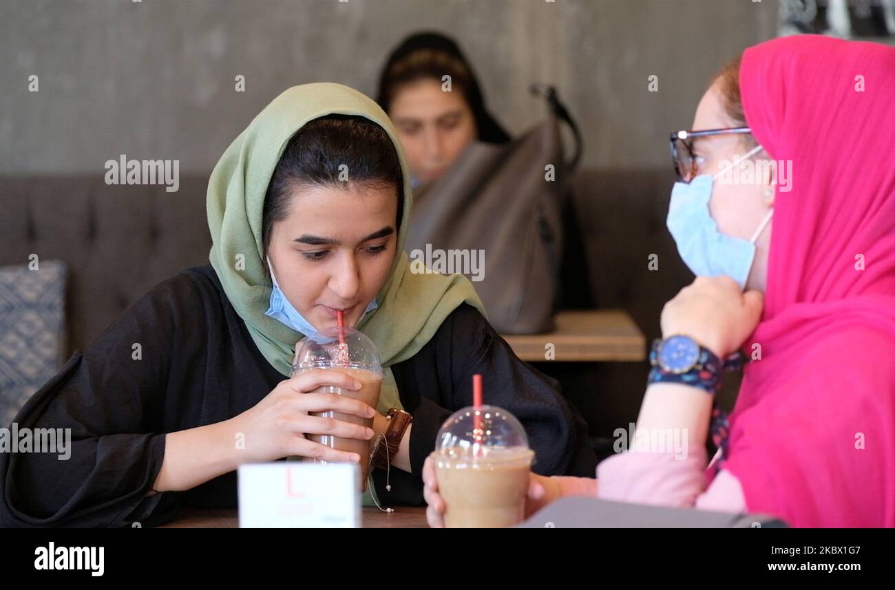 Two Iranian women wearing protective face masks sit at a cafe in ...