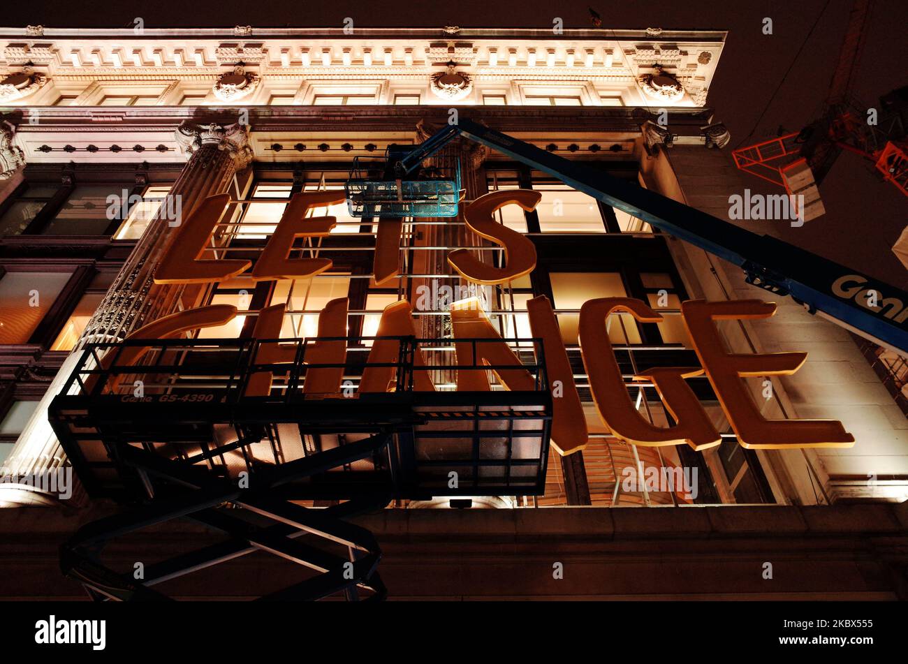 Workmen install giant lettering reading 'Let's Change' on the facade of ...