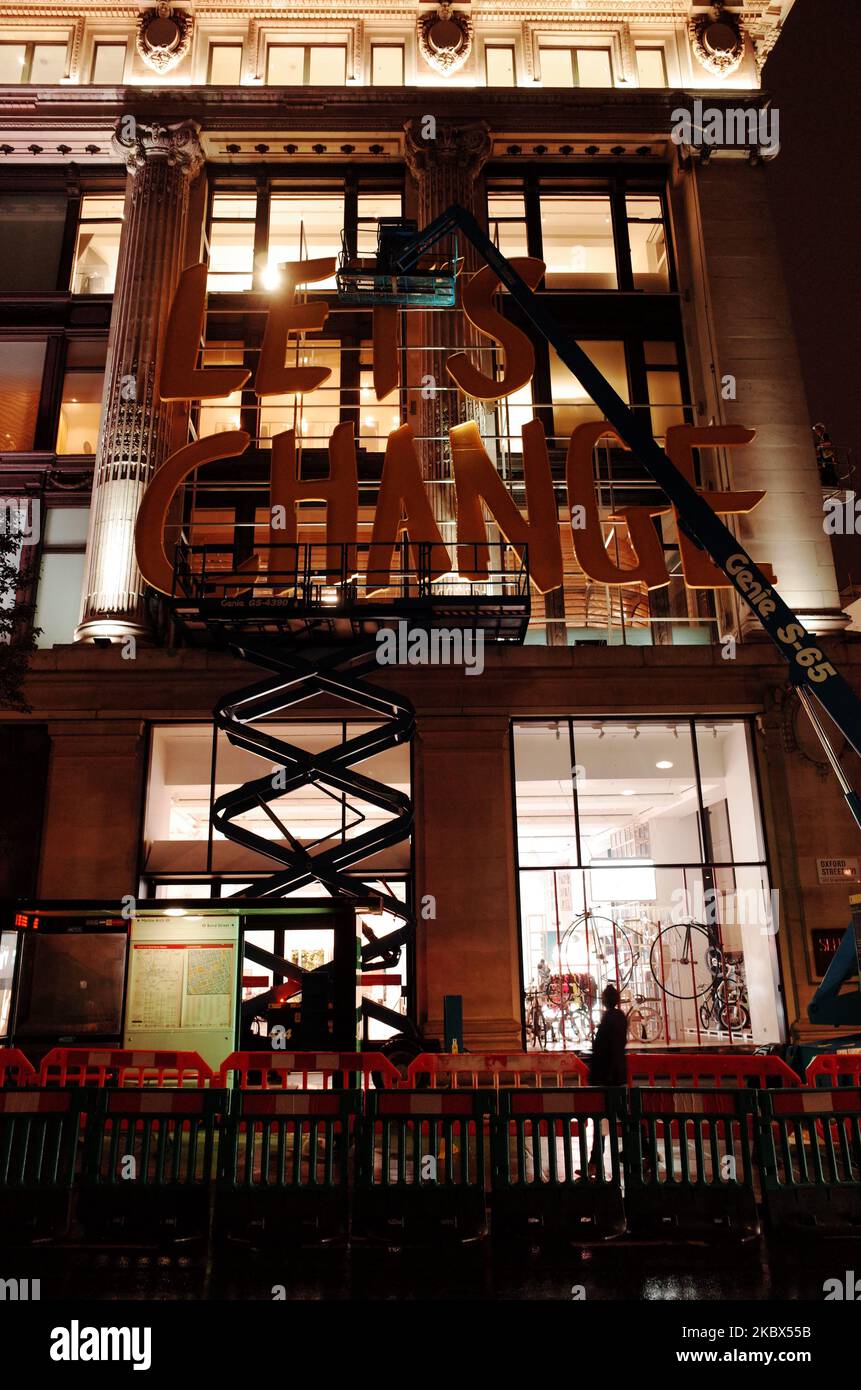Workmen install giant lettering reading 'Let's Change' on the facade of ...