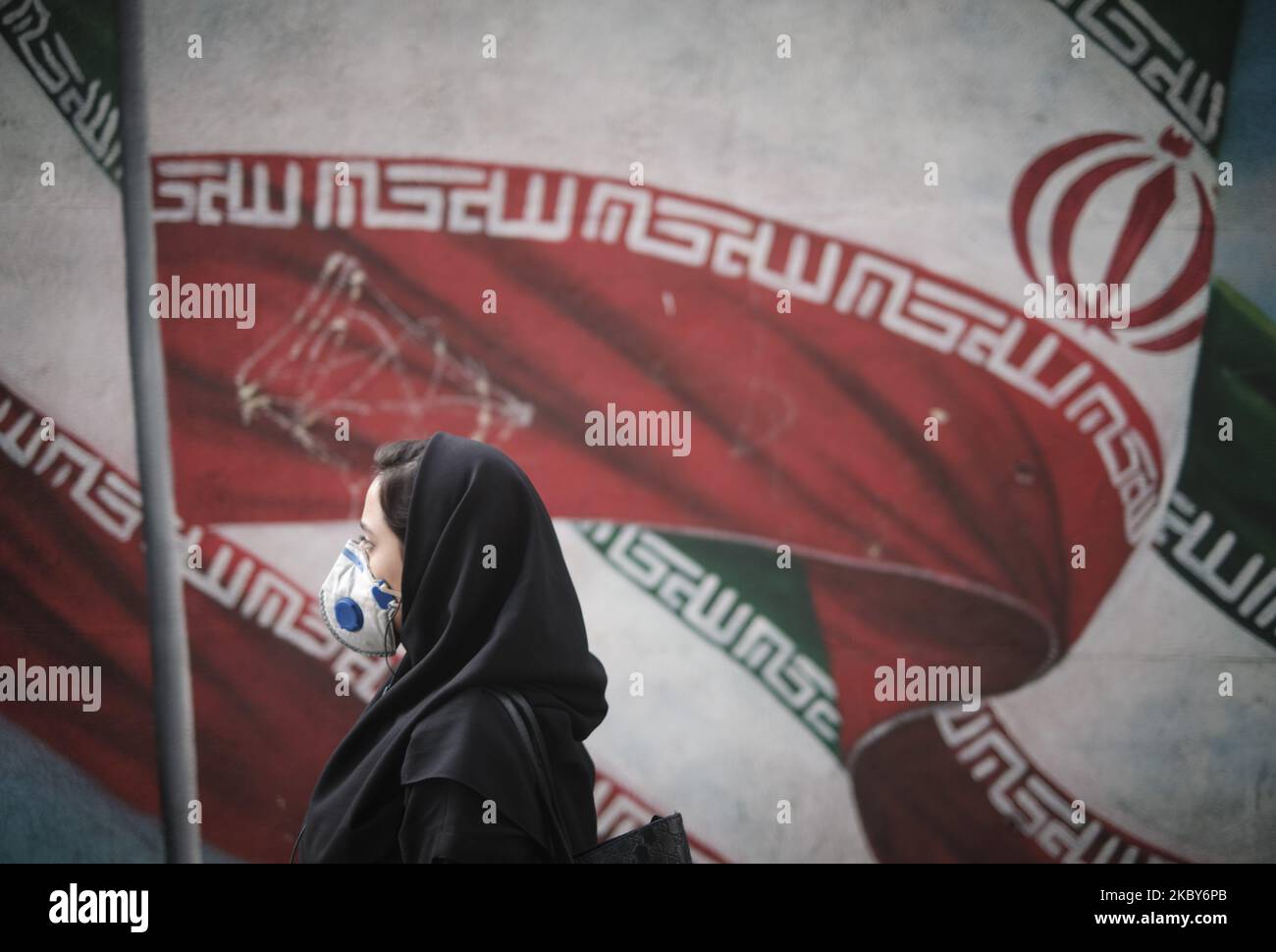 An Iranian woman wearing a protective face mask walks past an Iran flag ...