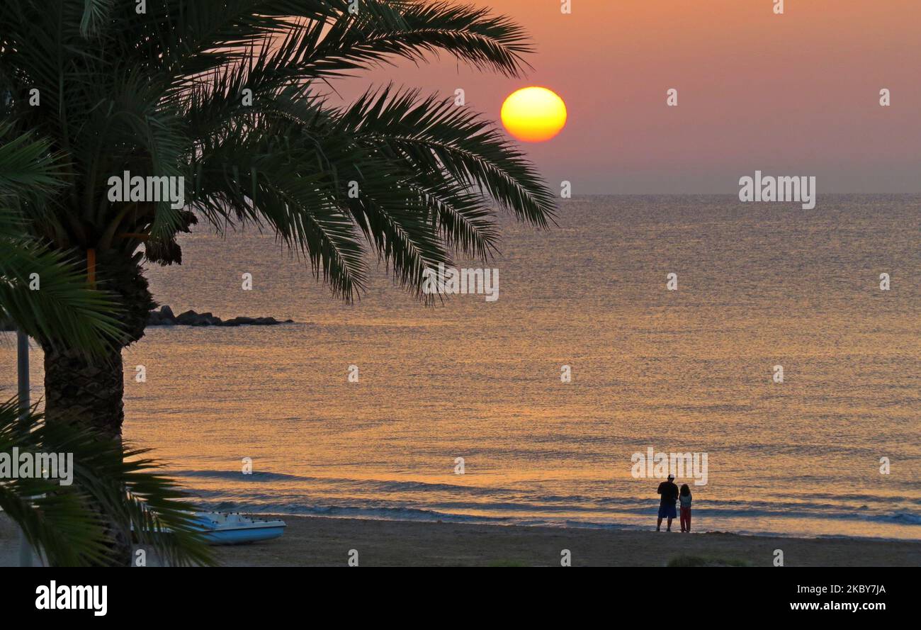 A mesmerizing scenery of a sunset over the beach with a couple enjoying ...