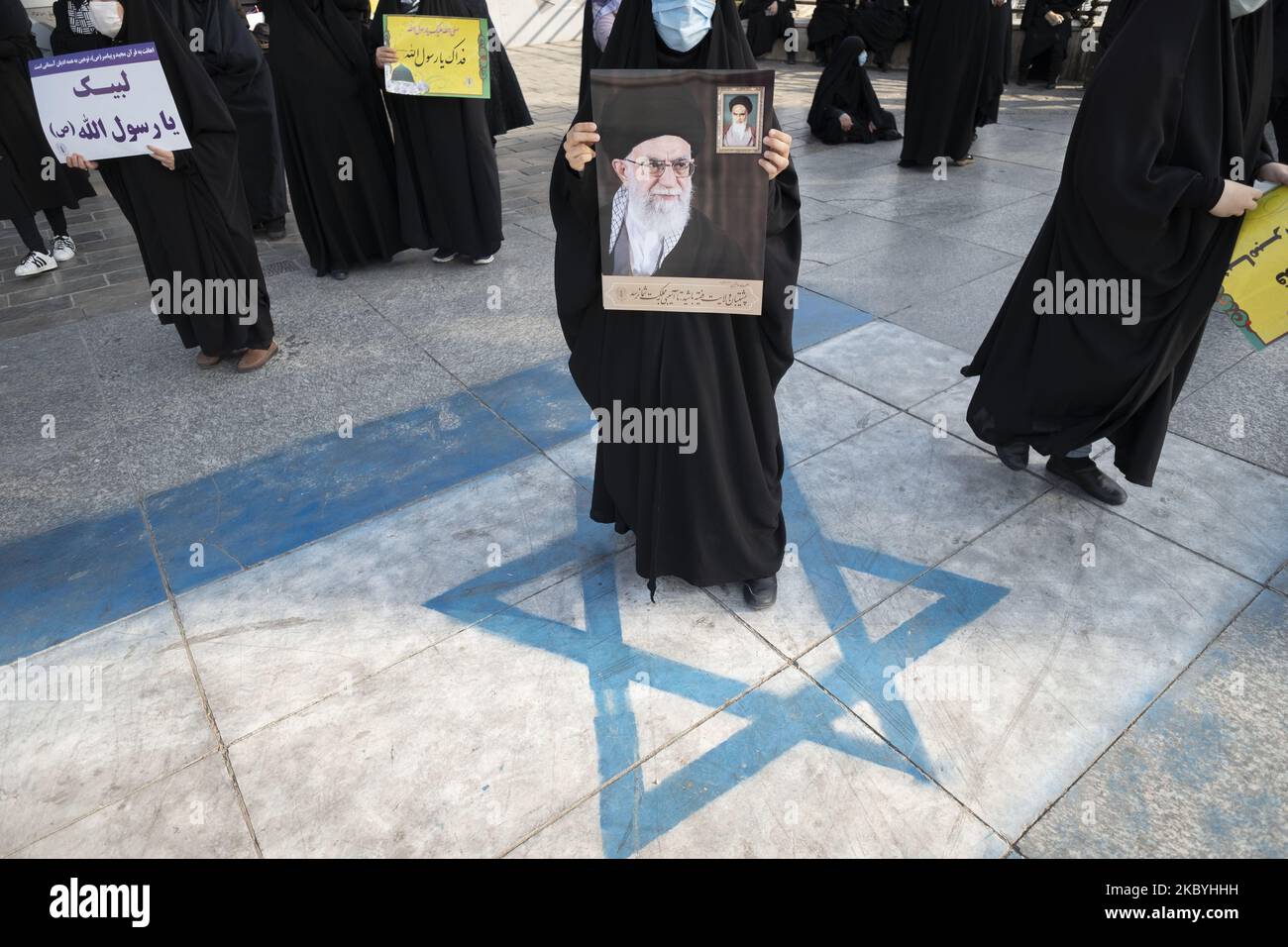 An Iranian veiled woman wearing a protective face mask holds portraits ...