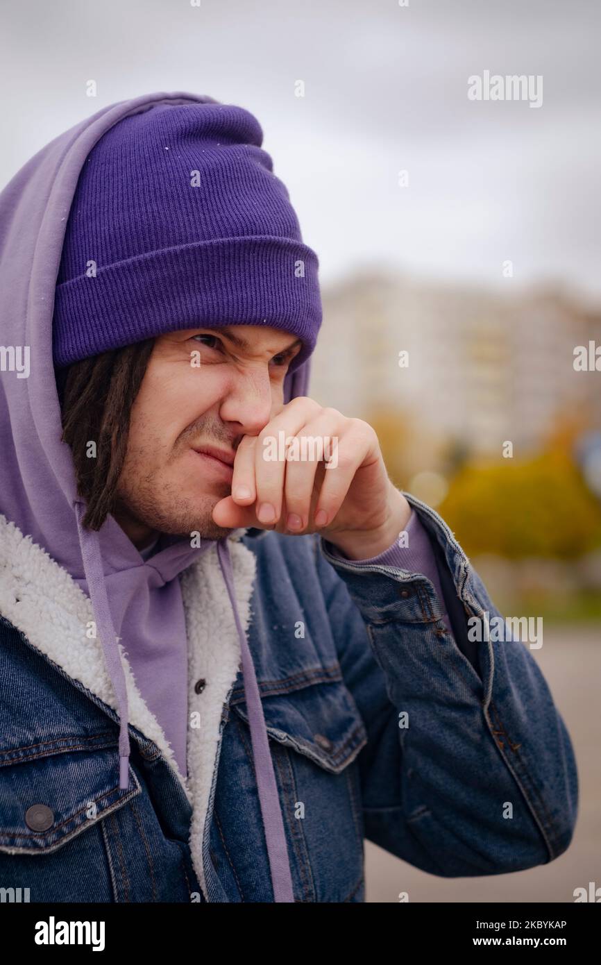 Portrait of man sniffling in cold weather, standing on city street ...