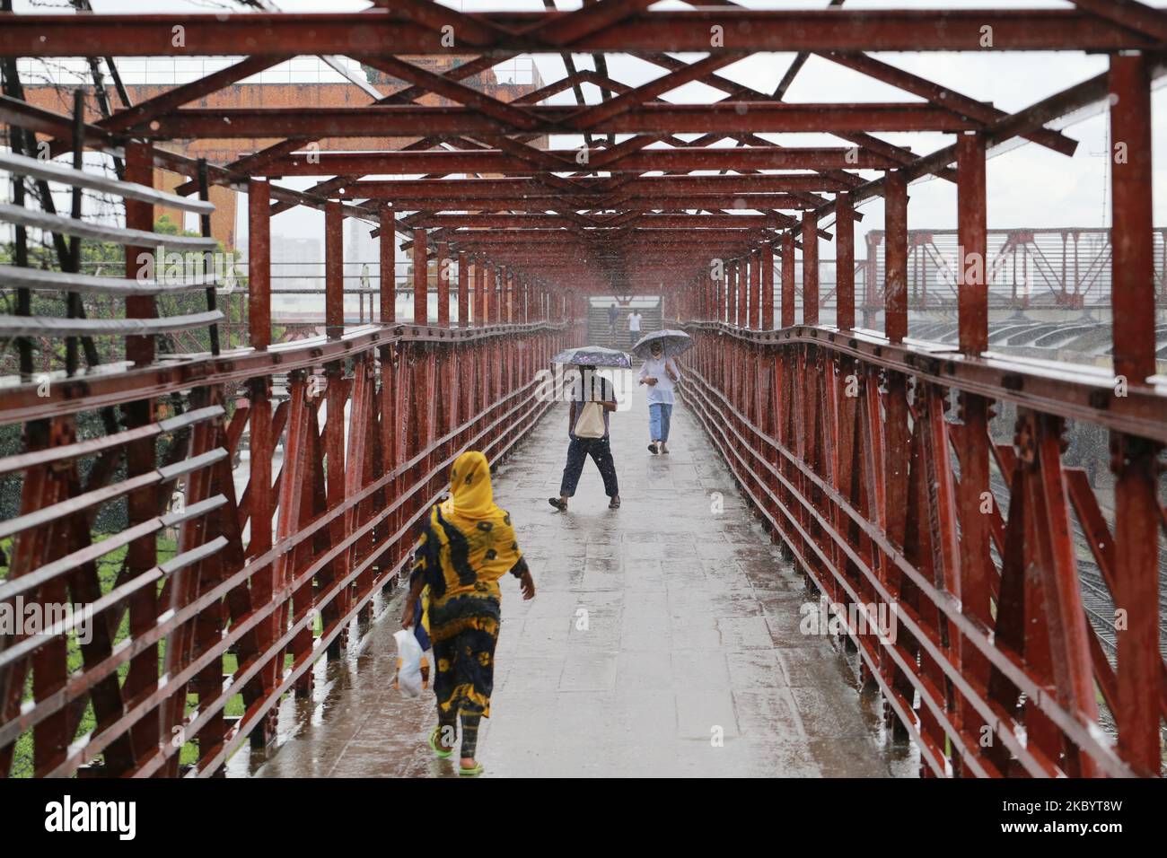 People walk on a foot over-bridge during the rainfall in Dhaka ...