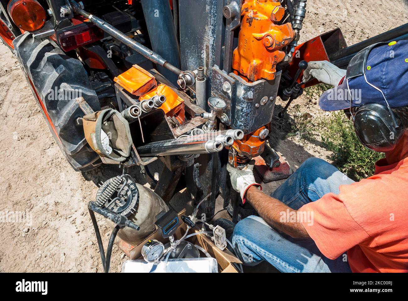 A male worker, wearing gloves and hearing protectors, is working with ...