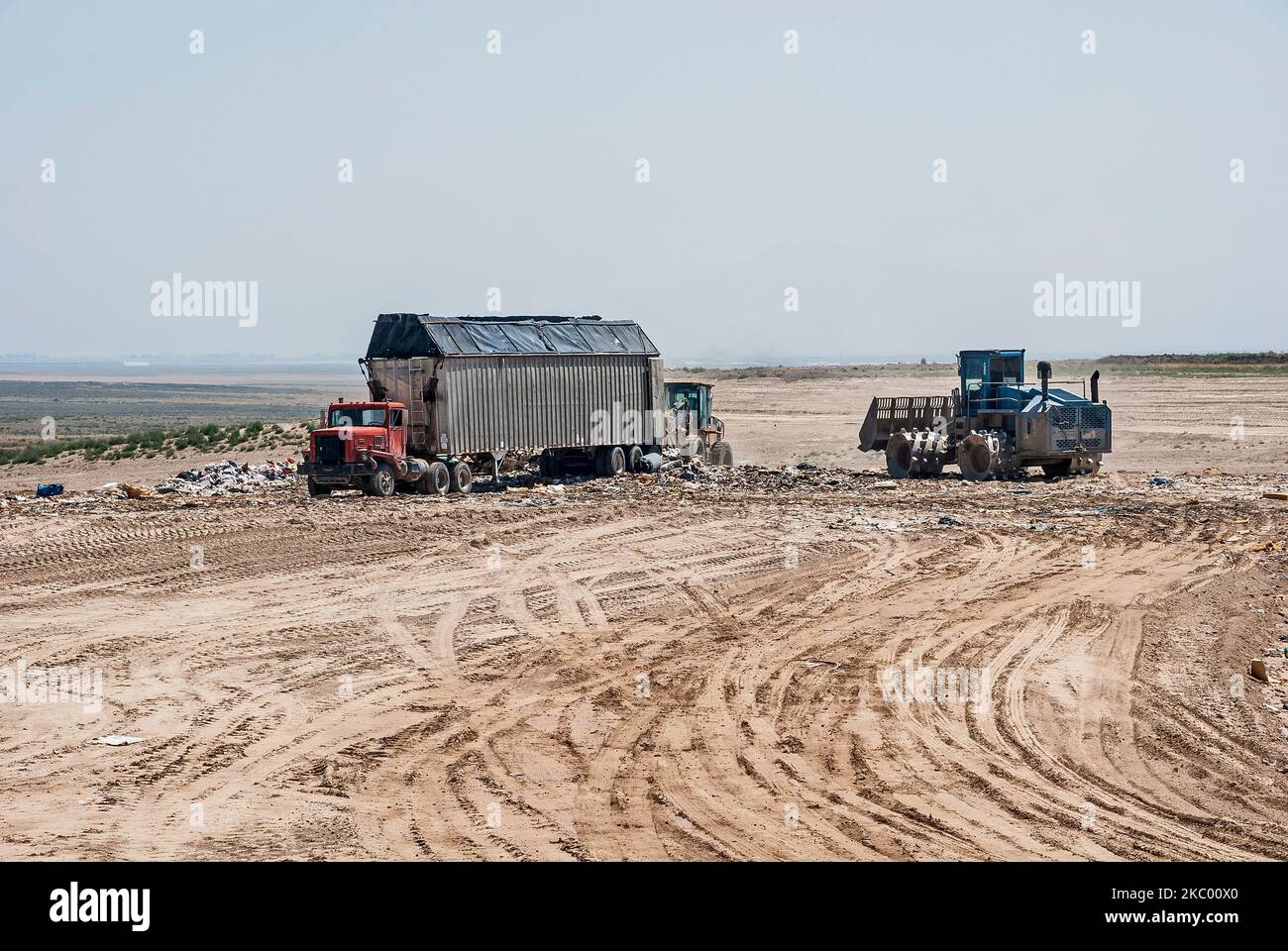 A tractor-trailer semi and two soil compactors on flat land in an ...