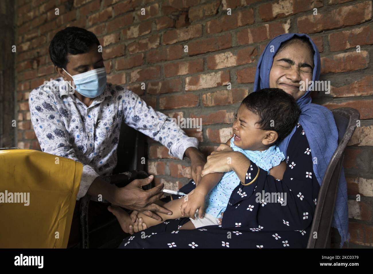 A health assistant applies a vaccine to a child in a rural area of ...