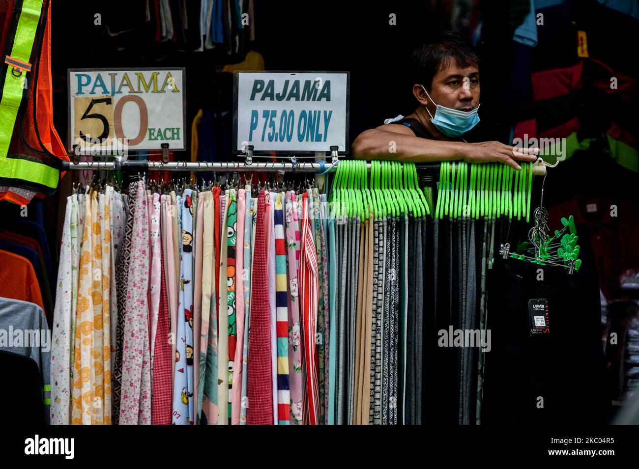 A man wearing a face mask tends to a clothing stall at a public market ...