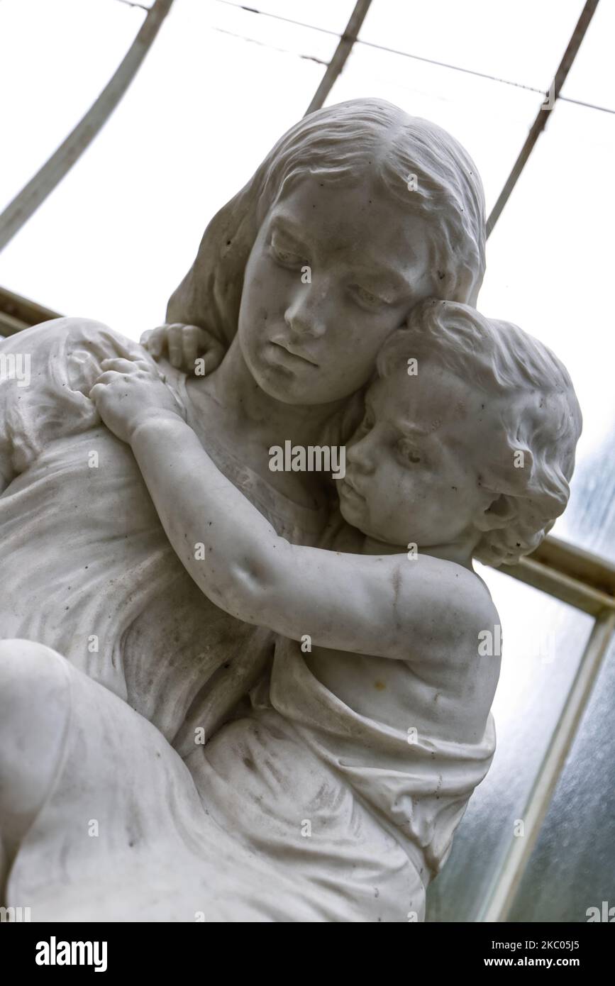 A vertical shot of a white statue of a mother holding her son in a ...