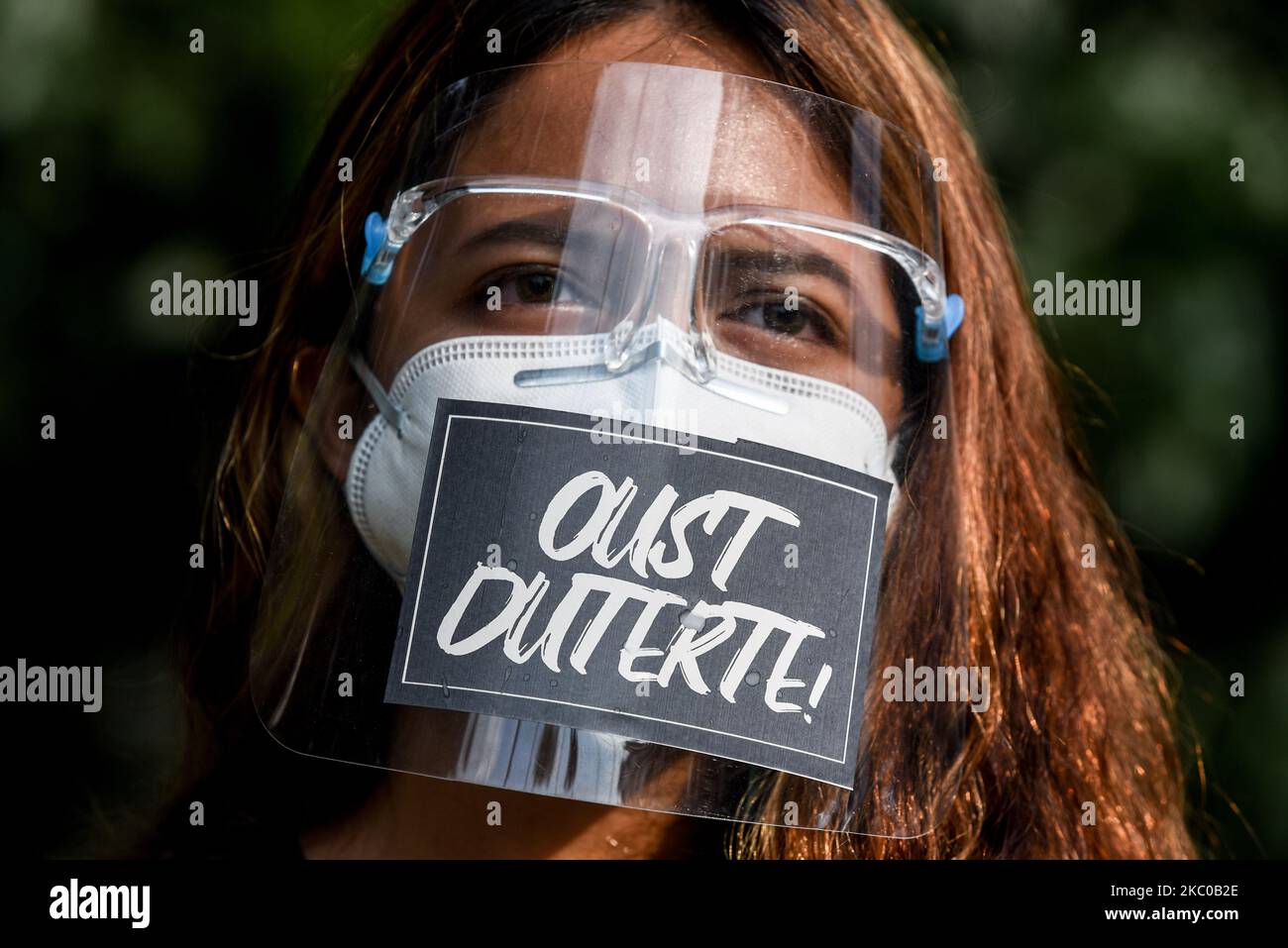 A woman wearing a face mask and a face shield with the text "Oust ...