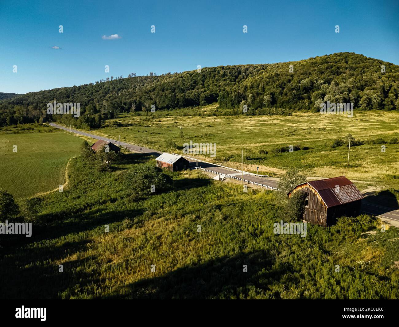 The drone view of the barns in the green field with the forest hills ...