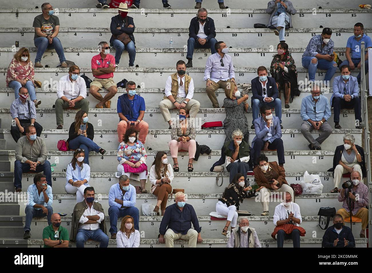 People are seen sitting in the stands, wearing face masks and keeping ...