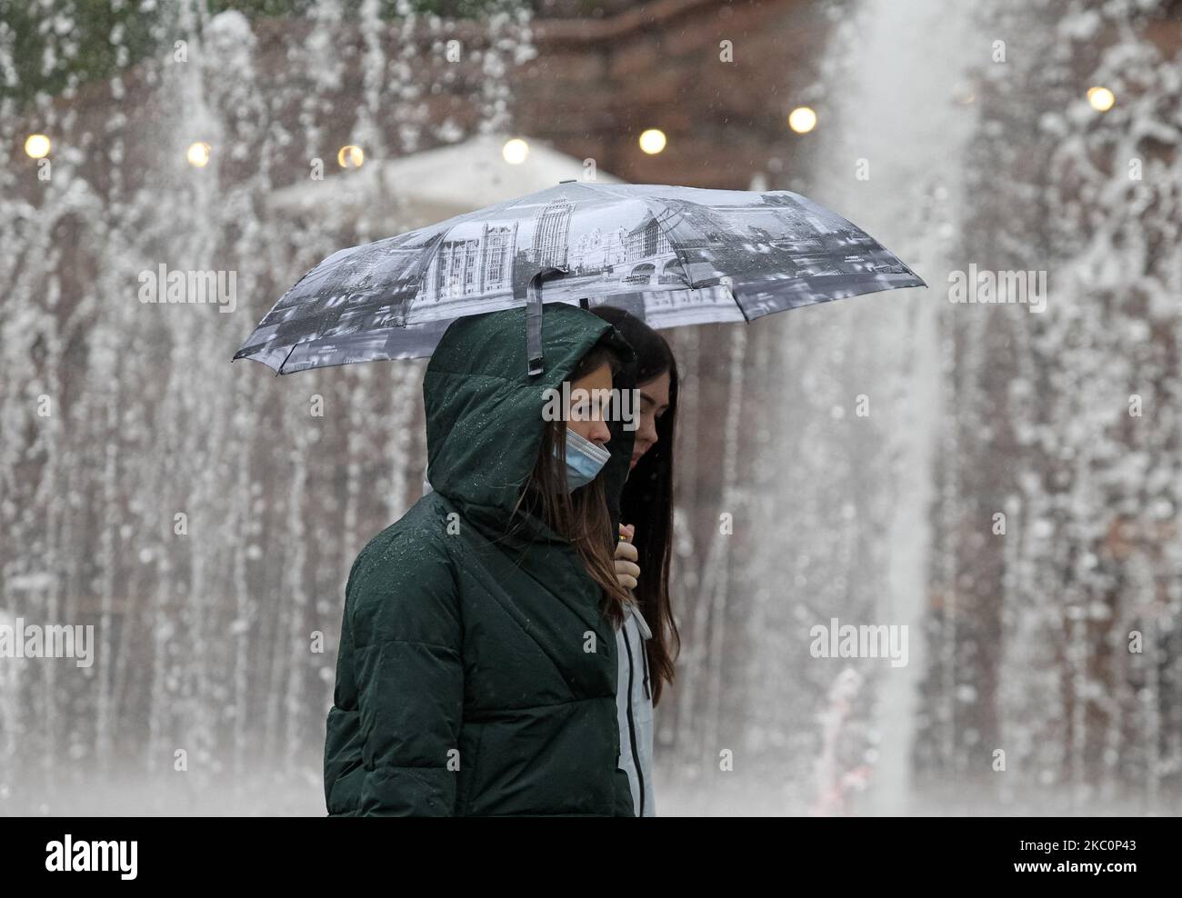 Women with umbrellas walk past the city fountain during rain in the ...